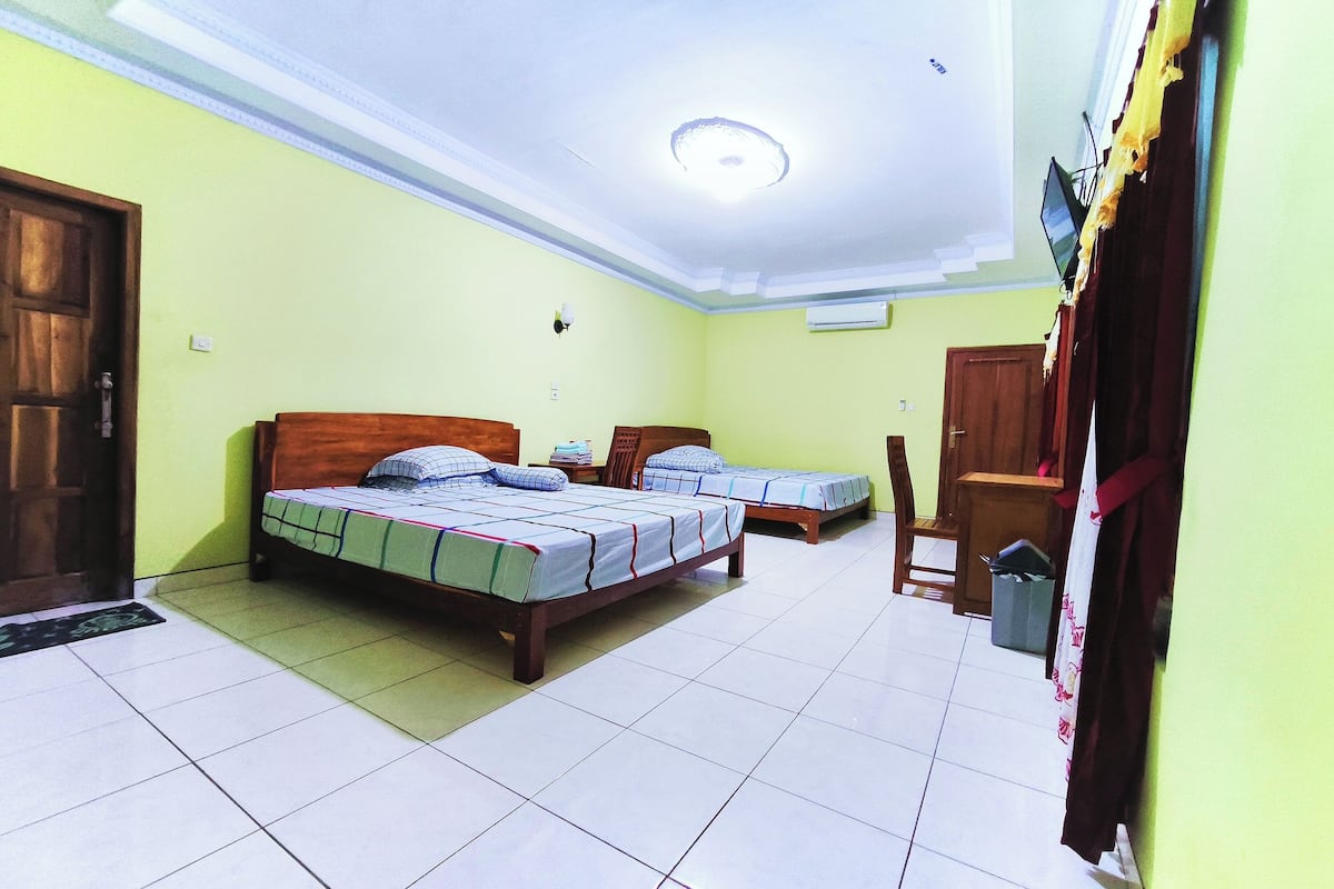 Quarto com duas camas, uma escrivaninha, uma cadeira, uma porta e um ar condicionado.