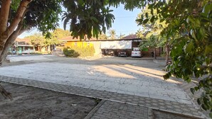 Um pátio pavimentado com um edifício amarelo, carros estacionados e uma árvore.