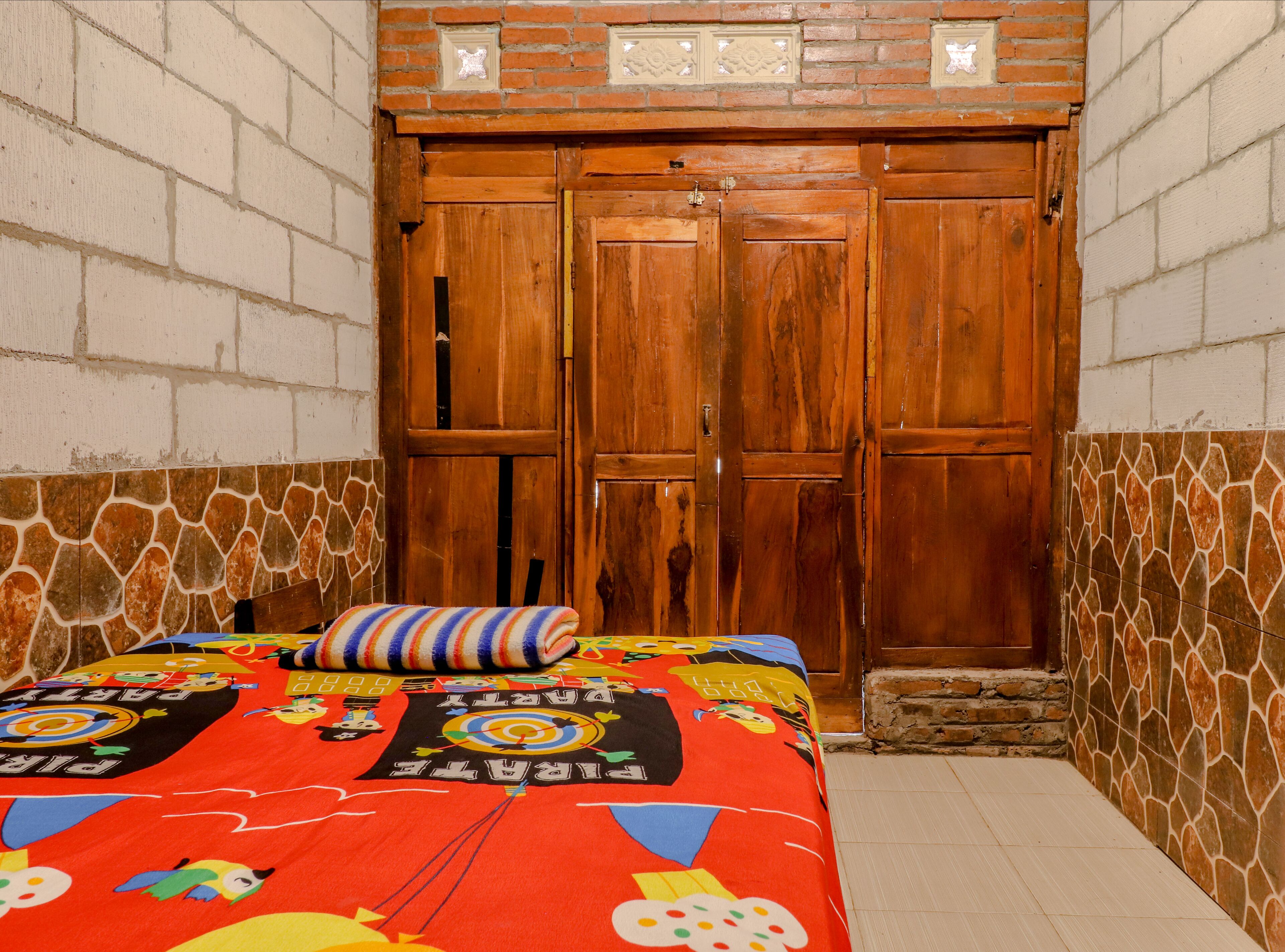 Quarto pequeno com cama, guarda-roupa de madeira e parede de pedra.