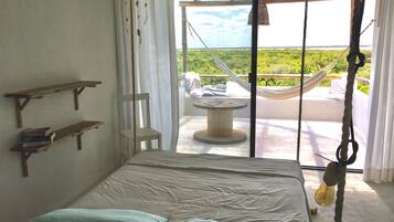 Quarto com cama, almofadas, uma cadeira, uma mesinha e uma rede lá fora da janela.
