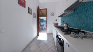 Uma cozinha com armários brancos, um fogão e uma pia. Há um relógio na parede e uma porta que dá para outro cômodo.
