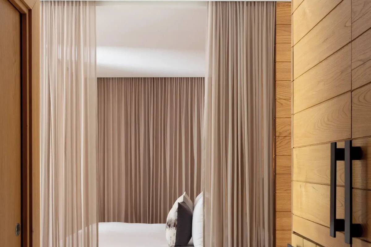 Quarto com cama, guarda-roupa de madeira e cortinas leves.