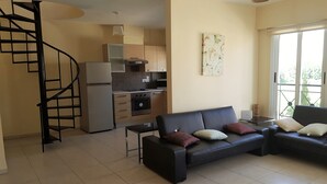 Uma sala de estar moderna com um sofá de couro preto, uma mesinha e uma escada em espiral que dá acesso a uma cozinha.