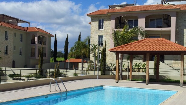 Piscina com escada de metal, cercada por um deck revestido com azulejos.