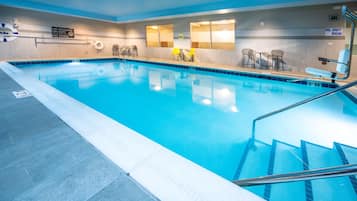 Uma piscina interior com divisórias de pistas bem definidas, posto de salva-vidas e placa indicando a capacidade da piscina.