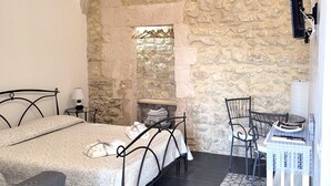 Quarto com parede de pedra, cama, poltrona, mesa pequena e lareira.