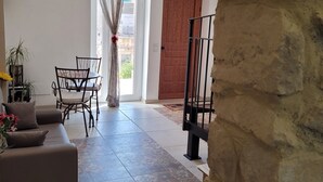 Uma sala de estar com sofá, mesa de jantar com cadeiras, escada e porta.