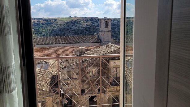Vista de varanda com grade de metal, mostrando um edifício histórico com uma torre de sino e telhados de terracota.