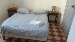 Uma cama com roupa de cama listrada, duas mesas de cabeceira com abajures e um chão xadrez.