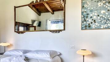 Quarto com uma cama, duas luminárias de cabeceira, um espelho grande e uma pintura floral na parede.