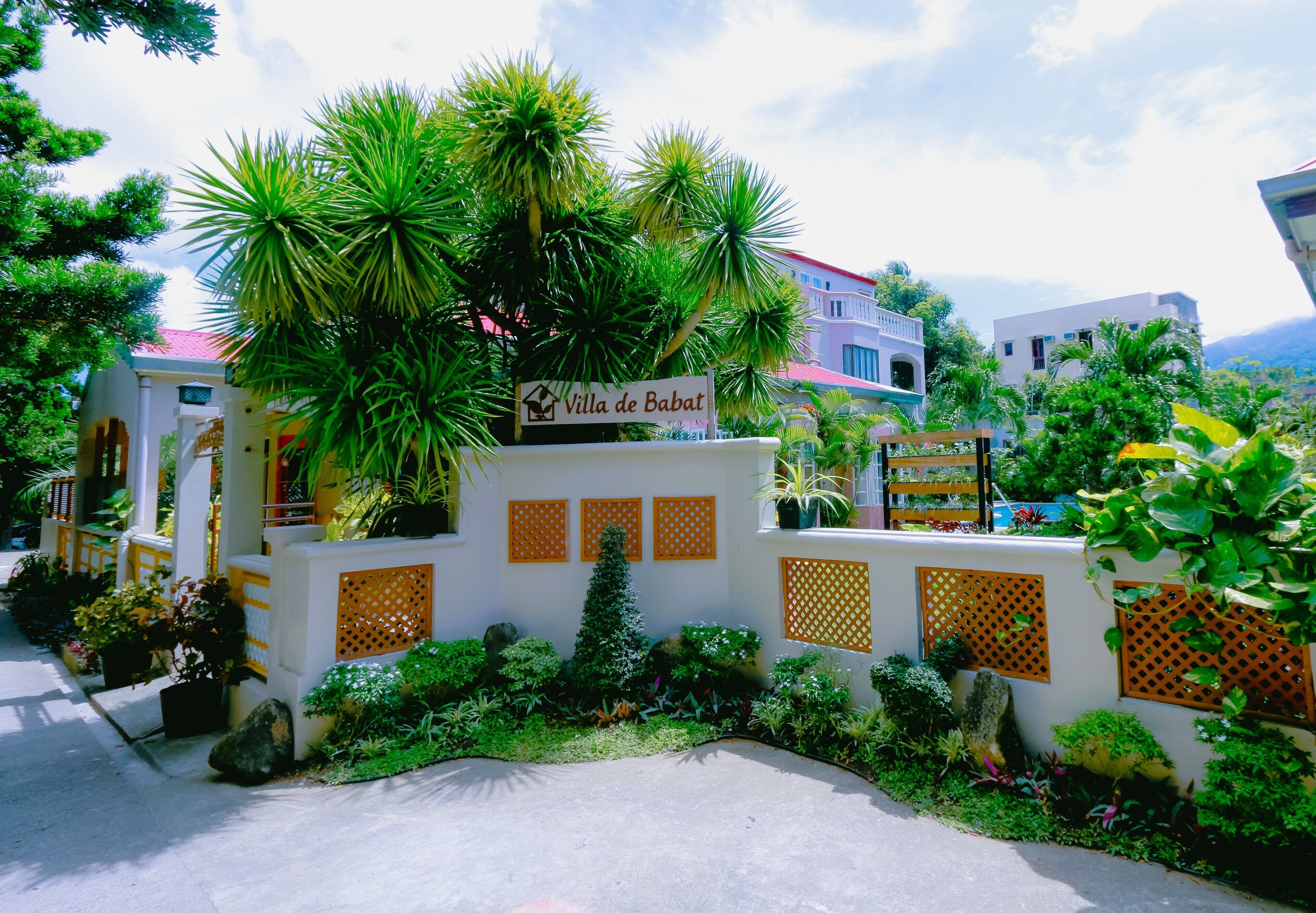 Villa de Babat com fachada branca, plantas tropicais e uma placa.