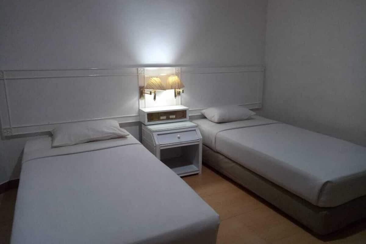 Quarto de hotel pequeno e individual, com duas camas, uma mesa de cabeceira e um abajur.