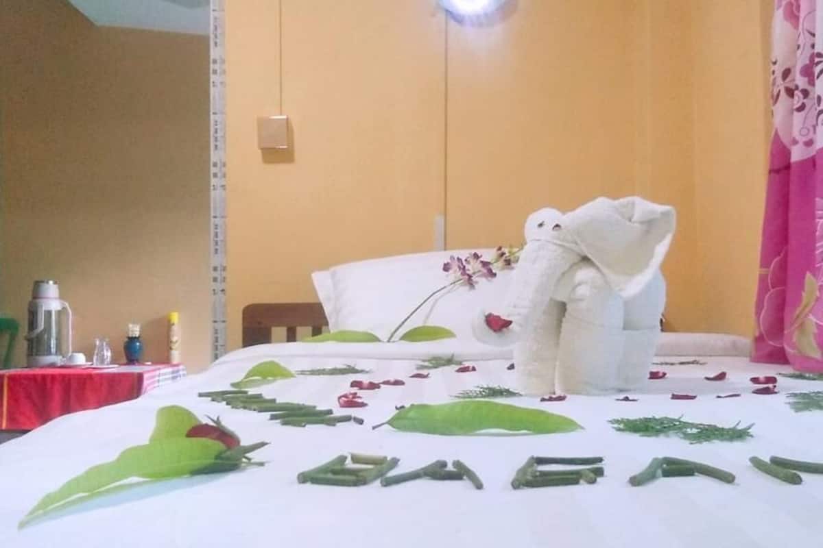 Quarto de hotel com cama coberta por lençóis brancos, arranjo de toalhas e uma mesa com folhas e flores verdes.