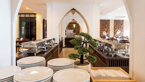Restaurante com arco central, serviço de buffet e uma árvore bonsai.