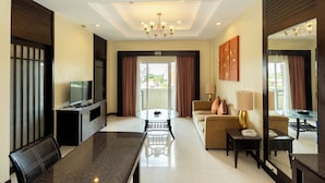 Quarto de hotel moderno com mesa de jantar, sofá, televisão e varanda com cortinas.