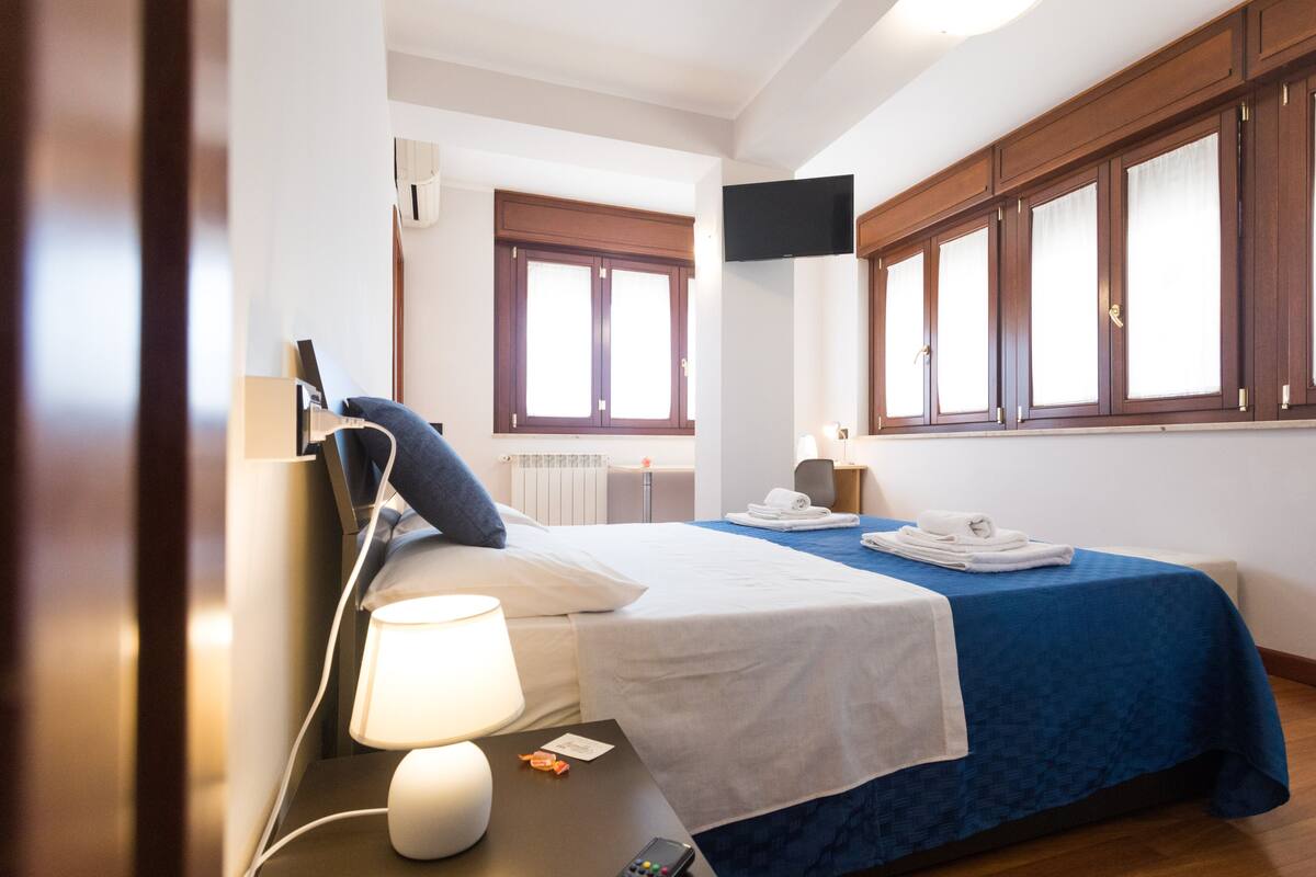 Quarto de hotel com cama, luminária de cabeceira, controle remoto e televisão de tela plana na parede.