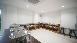 Quarto moderno e bem cuidado, com disposição de buffet, incluindo copos e pratos em prateleiras, um espaço para café e uma pequena mesa com cadeiras.