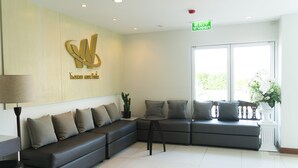 Uma área de recepção moderna com uma grande placa dourada, um sofá com almofadas, uma pequena mesa e um vaso de planta.