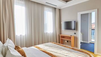Quarto de hotel com uma cama grande, televisão na parede e porta para uma varanda.