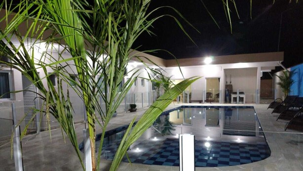 Uma área de piscina com piso xadrez, cercada por um pequeno muro e plantas em vasos.