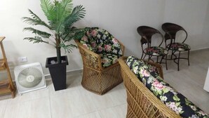 Quarto com móveis de vime, uma planta em vaso e um ventilador de chão.