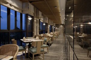 Um restaurante com mesas e cadeiras dispostas em fileiras, grandes janelas e design de interiores moderno.