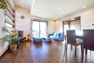 Uma sala de estar moderna com piso de madeira, um sofá azul, uma mesa de centro e uma TV. Há plantas em vasos e um espelho grande na parede.