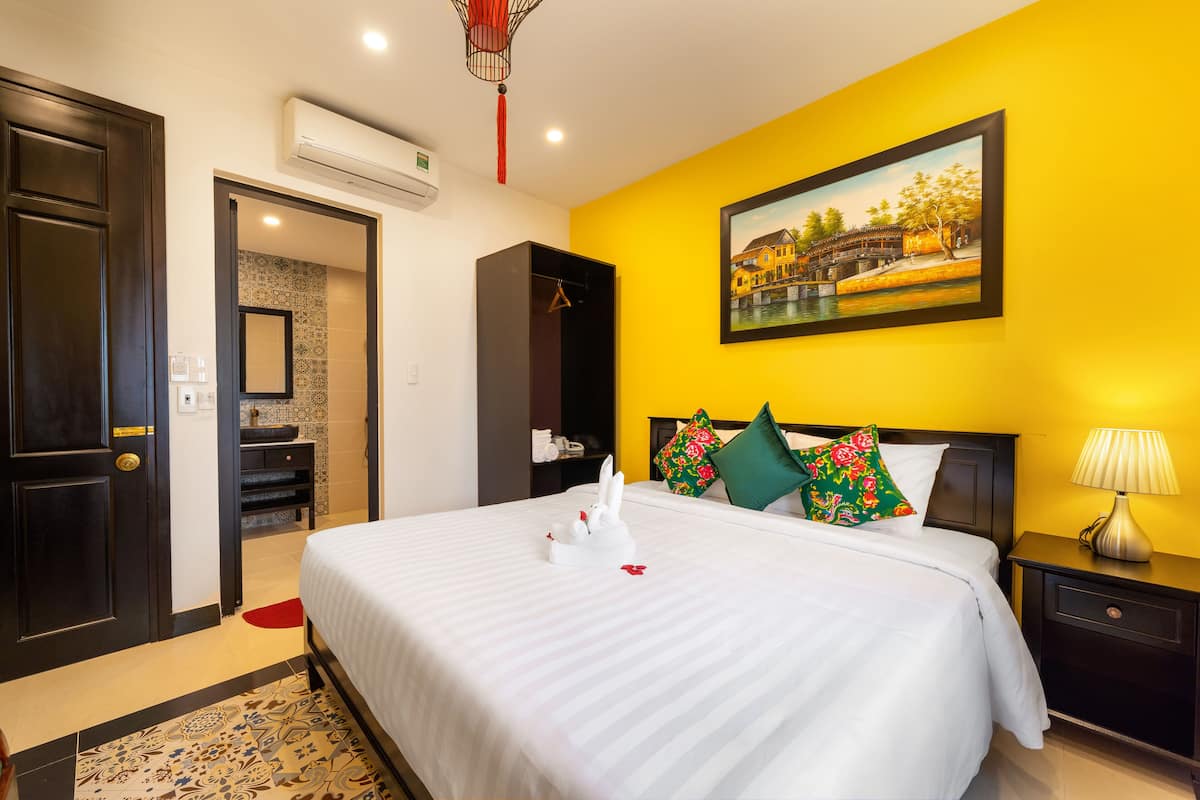 Quarto de hotel com cama, mesa de cabeceira, quadro pendurado na parede e porta.