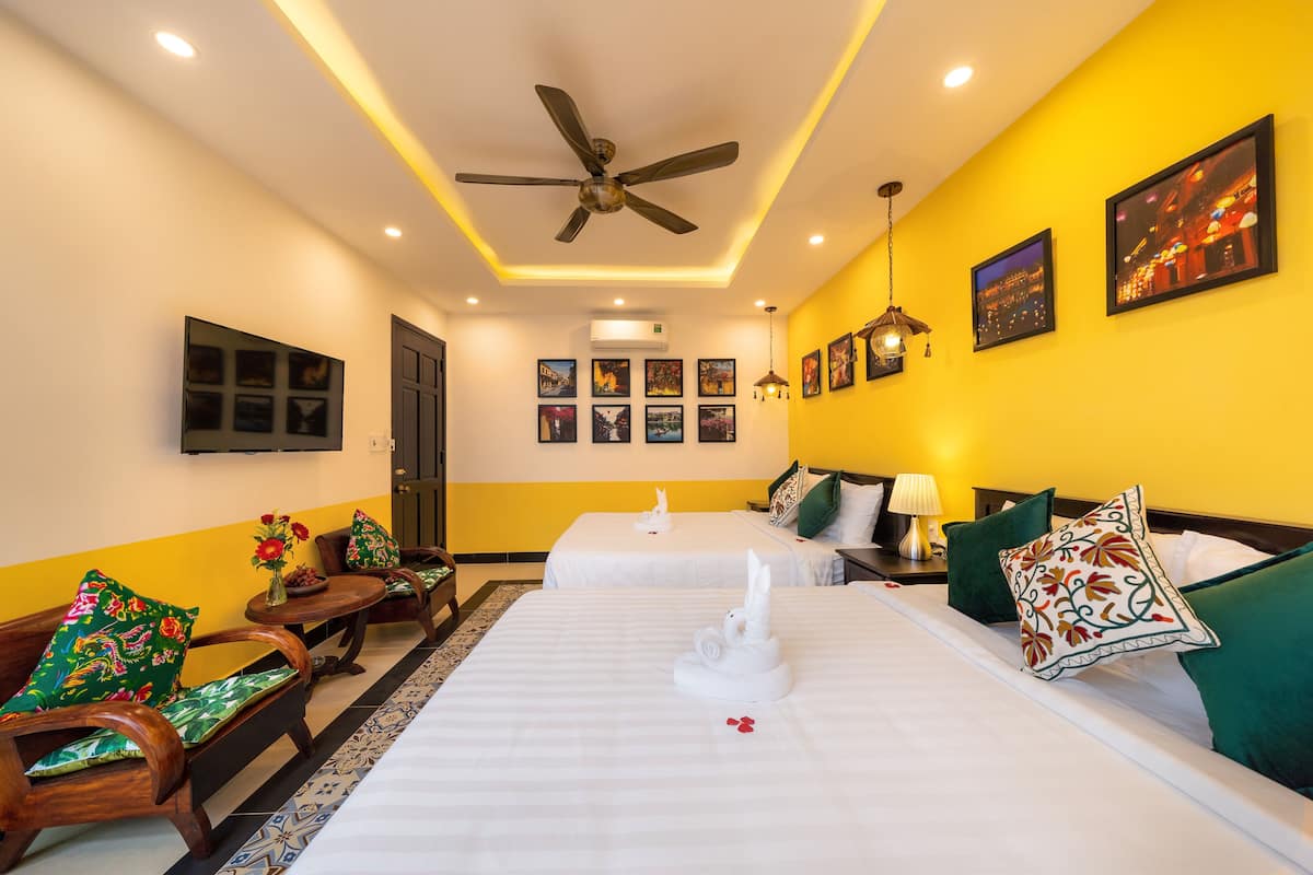 Quarto de hotel com duas camas, um ventilador de teto, televisão e obras de arte nas paredes.