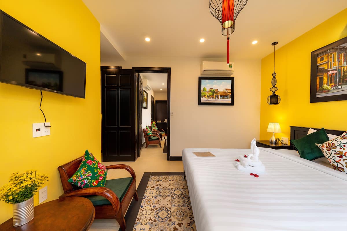 Quarto de hotel com cama, televisão, poltrona, mesa com um vaso e um quadro na parede.