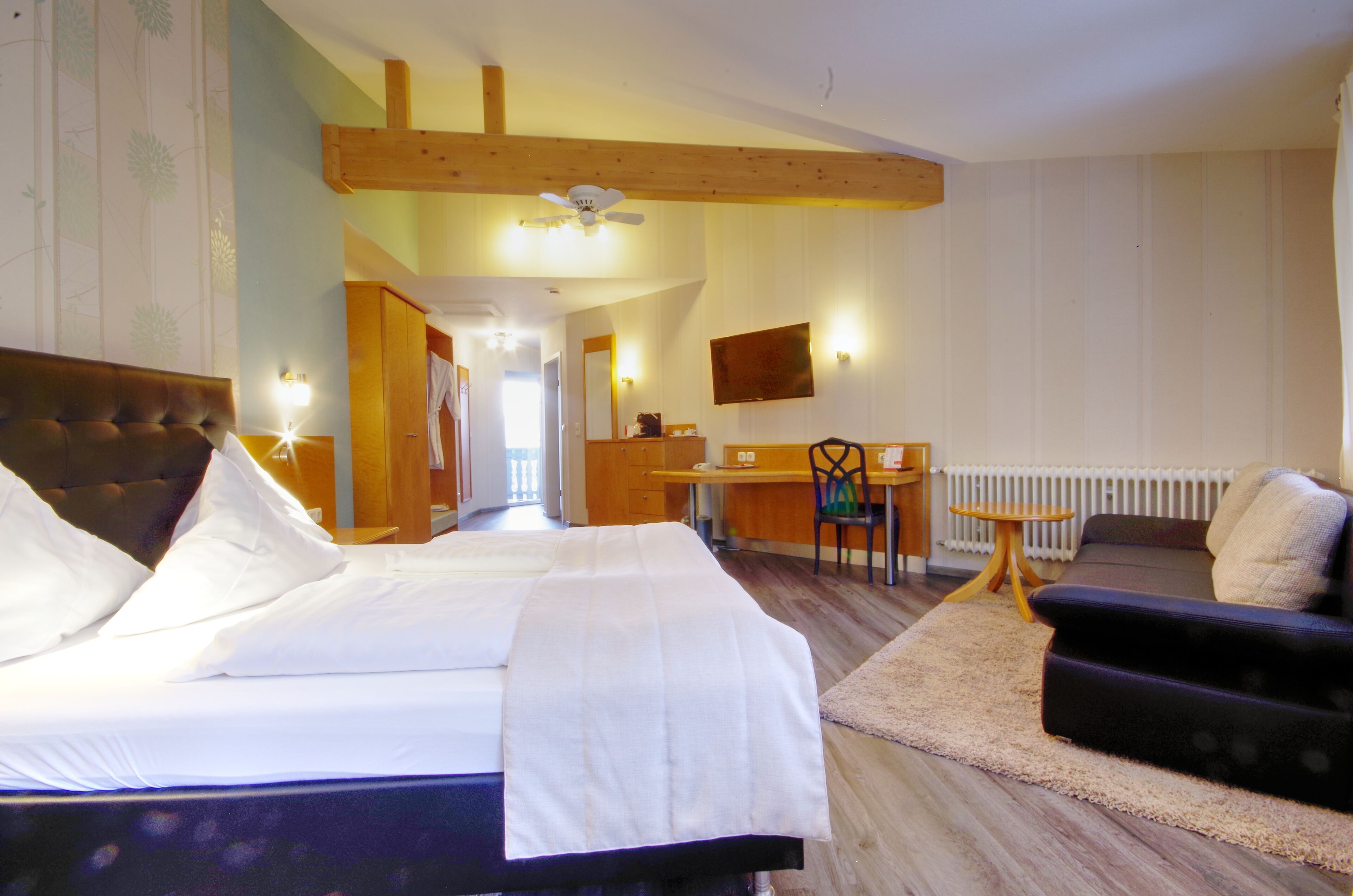 Quarto de hotel com cama grande, escrivaninha, cadeira, sofá e ventoinha no teto.