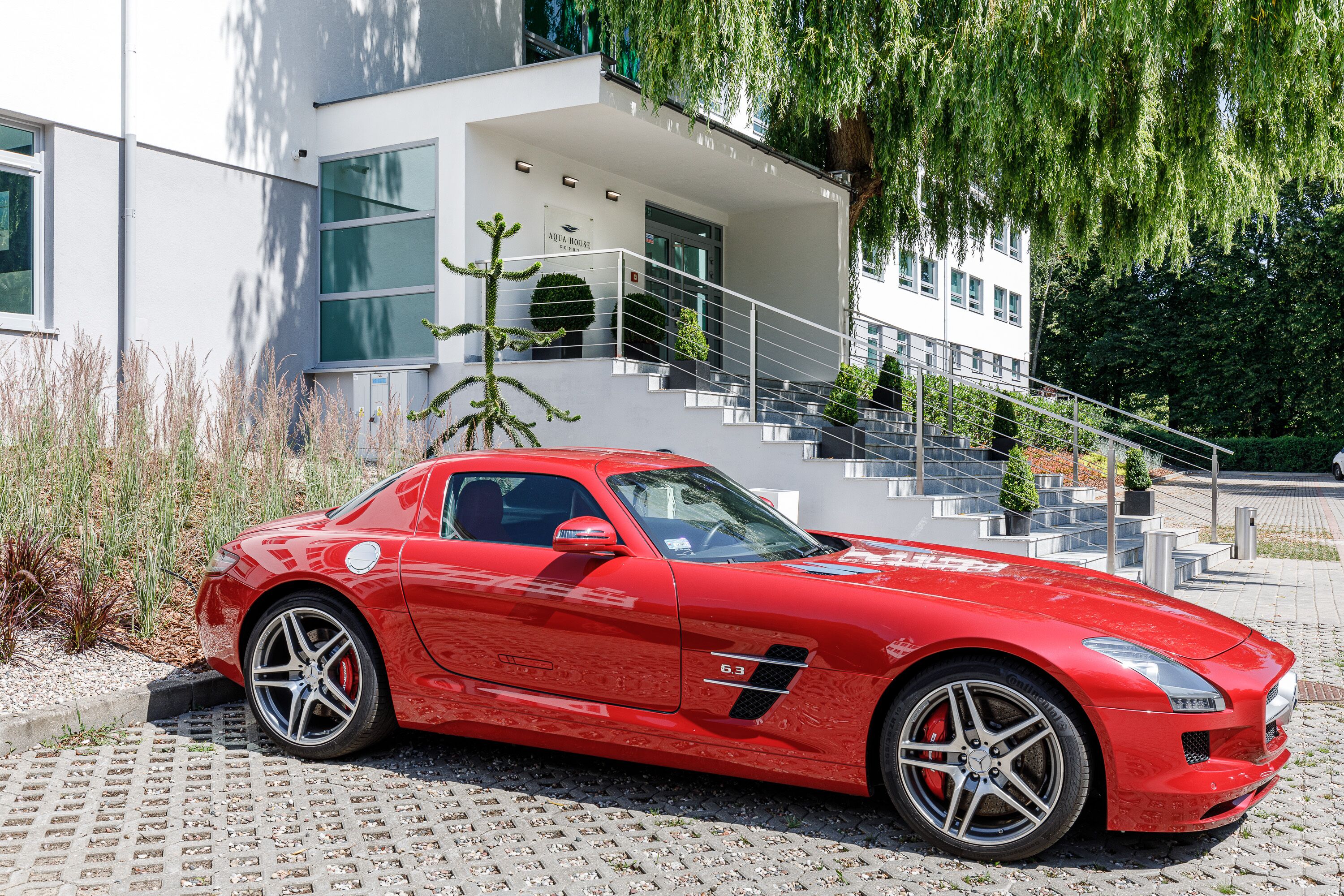 Um carro esportivo vermelho estacionado em frente a um edifício moderno com uma escadaria que leva à entrada.