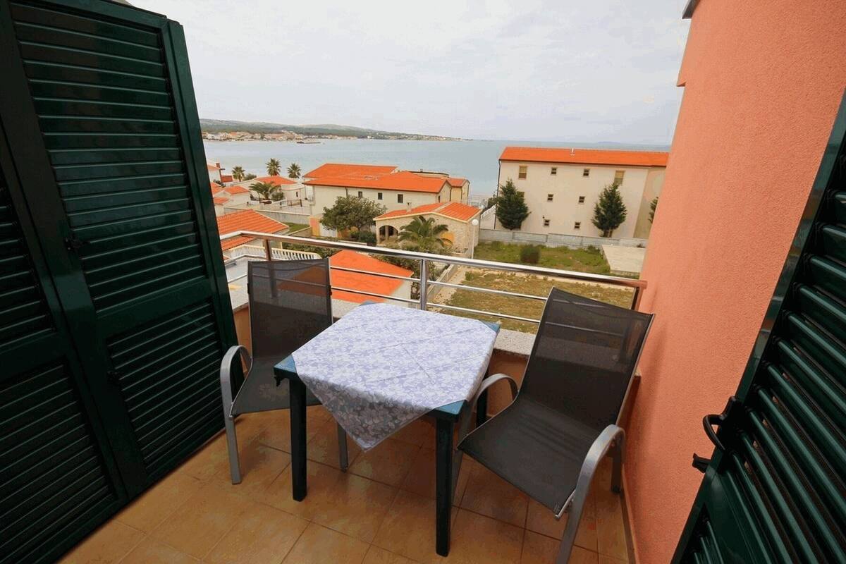 Varanda com mesa e cadeiras, com vista para uma cidade costeira com edifícios e um corpo de água.