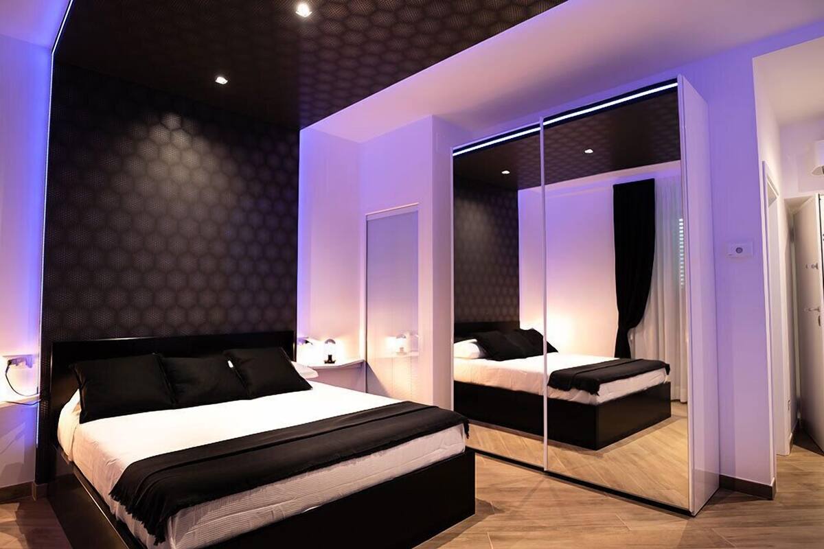 Quarto moderno com cama grande, guarda-roupa espelhado e iluminação ambiente.