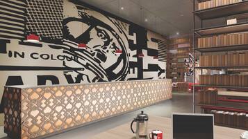 Uma biblioteca moderna com um grande mural na parede, uma estação de café e estantes de livros.