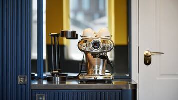 Uma máquina de café expresso antiga com duas xícaras sobre a plataforma, apoiada em um balcão com uma porta ao fundo.