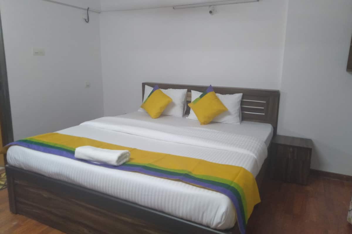 Cama bem arrumada com um cobertor colorido em tons de arco-íris e duas almofadas amarelas.