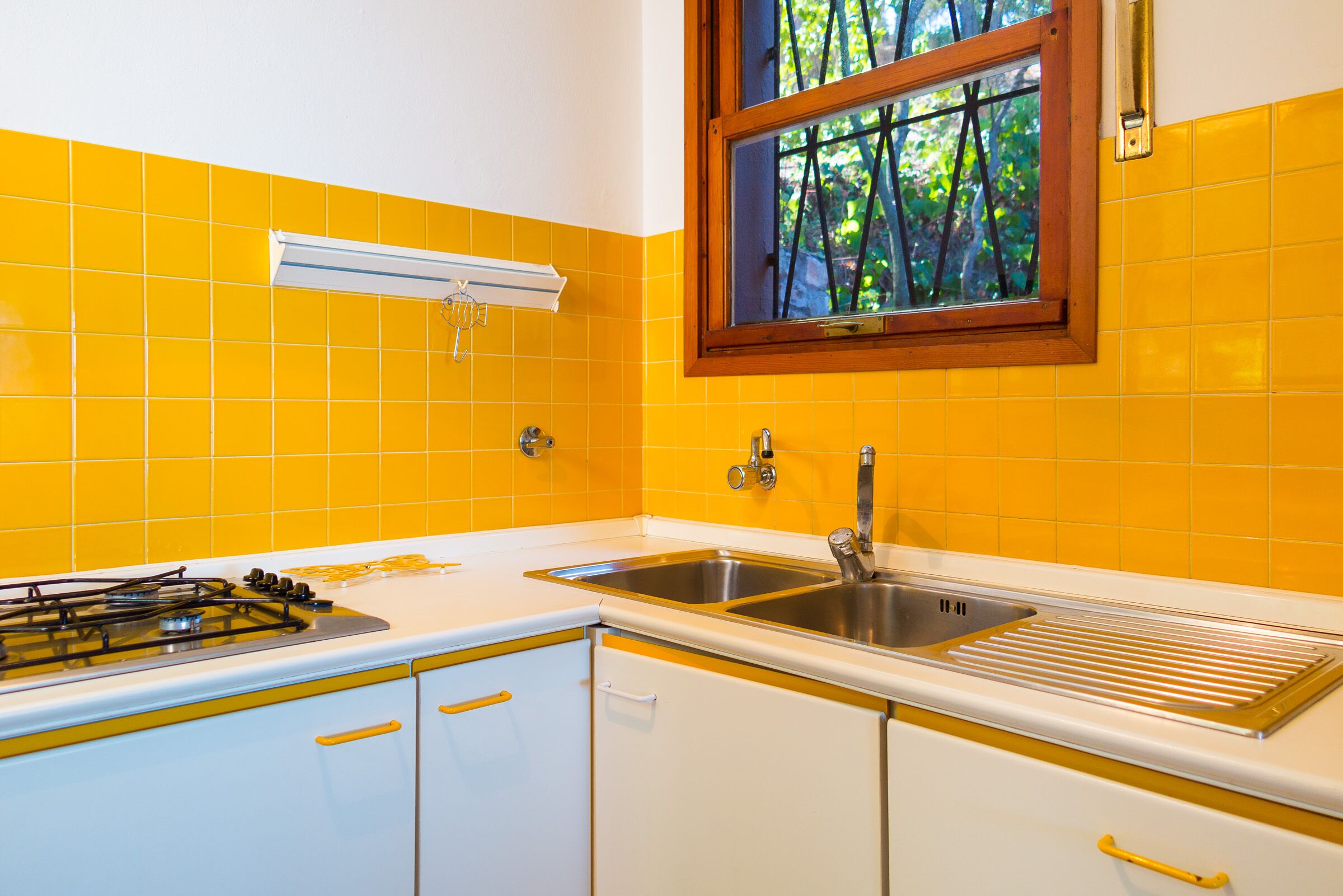 Uma cozinha com azulejos amarelos, uma janela, uma pia e um fogão.