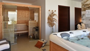 Um espaço de spa com sauna de madeira, hidromassagem e área de massagem com paredes de vidro.