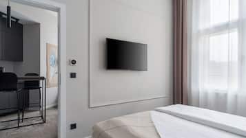 Quarto de hotel com cama, televisão de tela plana na parede, escrivaninha com cadeira e janela com cortinas.
