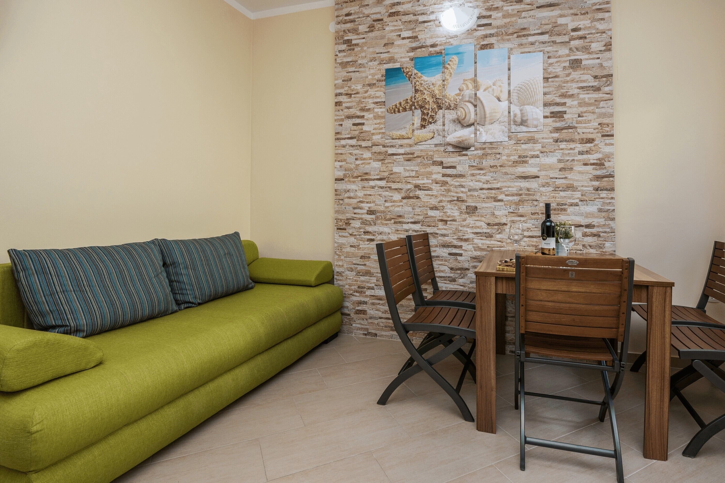 Quarto com sofá verde, mesa de jantar de madeira e cadeiras. Uma parede de pedra com obras de arte.