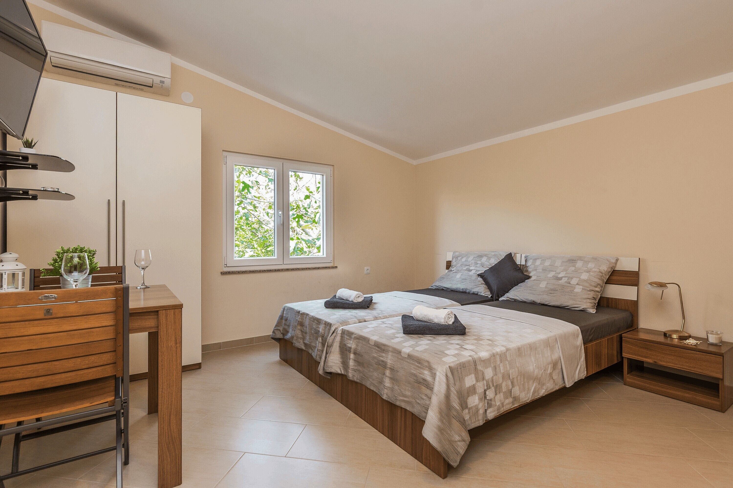Quarto com cama, mesa de cabeceira, luminária e janela com vista para vegetação.
