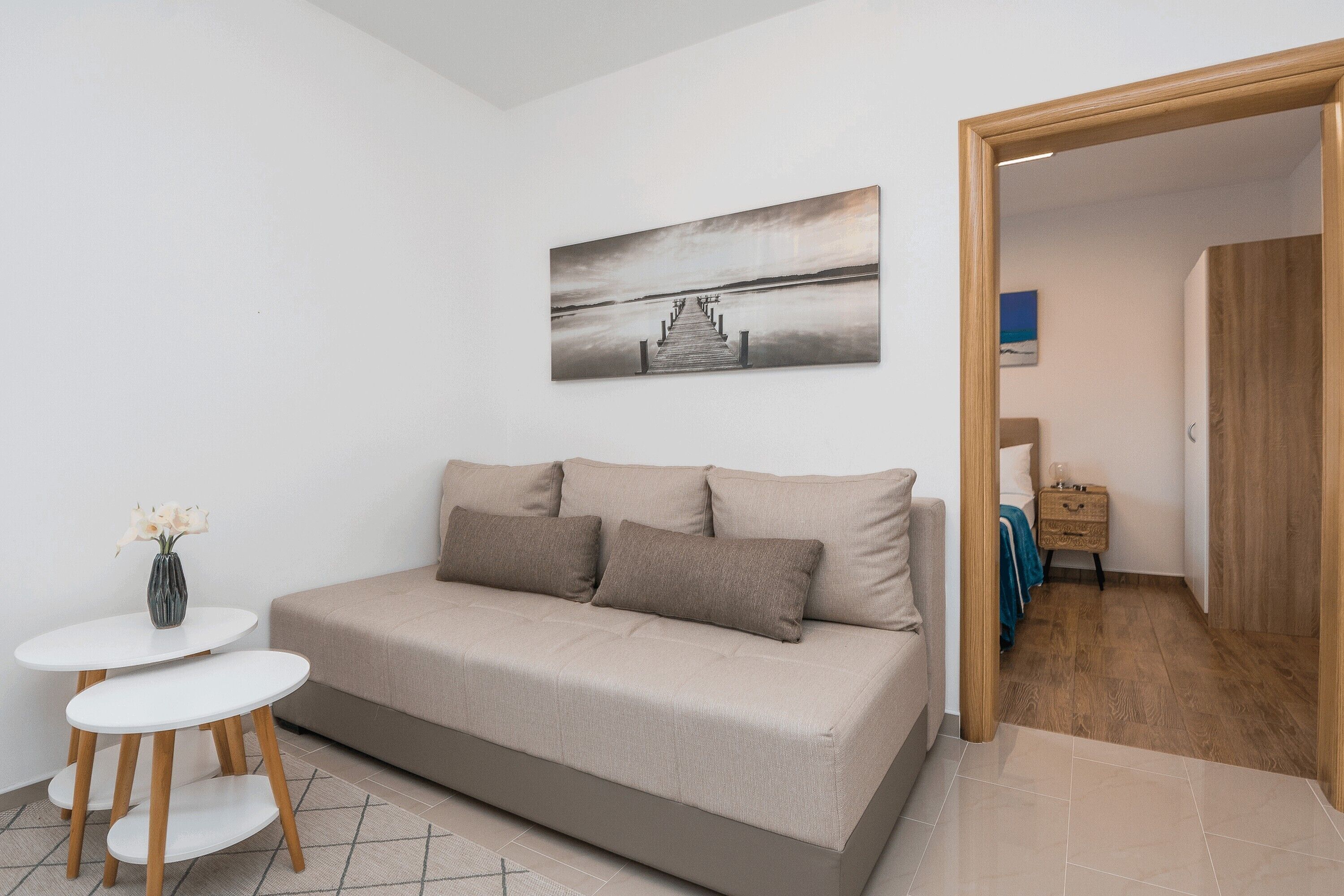 Uma sala de estar moderna com um sofá, uma mesinha e uma pintura de um cais.