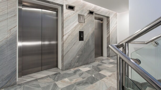 Um elevador moderno com portas metálicas e parede de mármore.