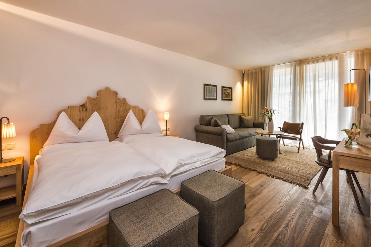 Quarto de hotel com uma cama grande, um sofá, uma mesinha e uma televisão.