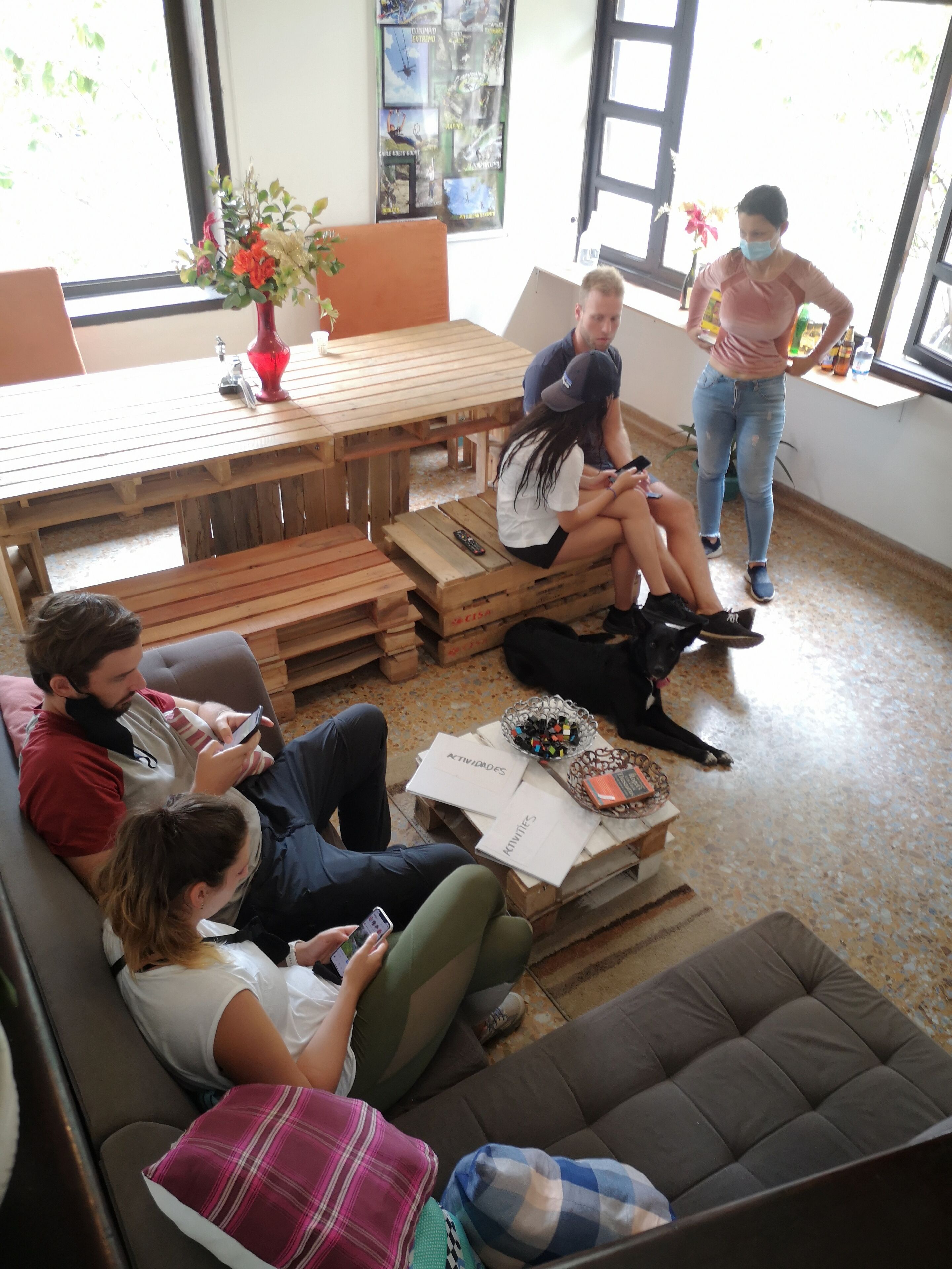 Um grupo de pessoas em uma sala com uma mesa de madeira, bancos e um cão.