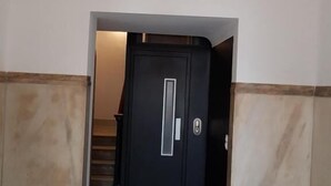 Um corredor com uma porta escura, um candeeiro em cima e chão de azulejos.