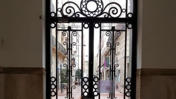 Um portão de ferro forjado preto com desenhos detalhados, dando acesso a uma vista da rua.