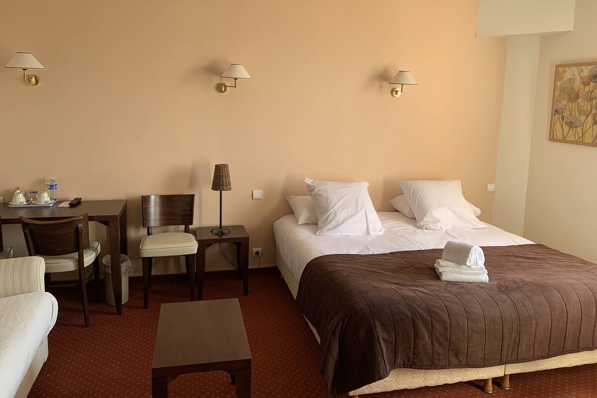 Quarto de hotel com cama, duas mesas de cabeceira, escrivaninha, cadeira, abajur e um quadro na parede.