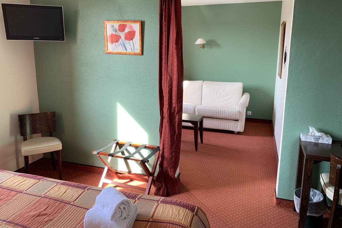 Quarto de hotel com cama, uma cadeira, um sofá, televisão, quadro e abajur.